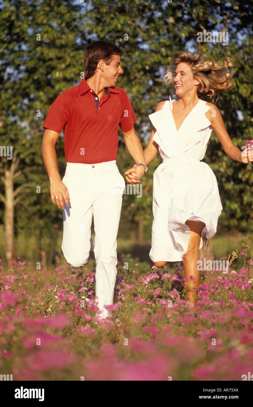 Romantic couple age 20s running together thru field of flowers holding ...