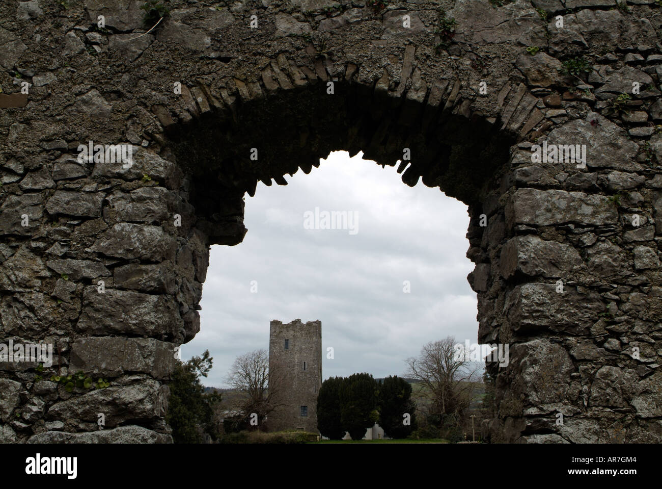 Old norman castle and leafless trees viewed through a dry stone archway ...