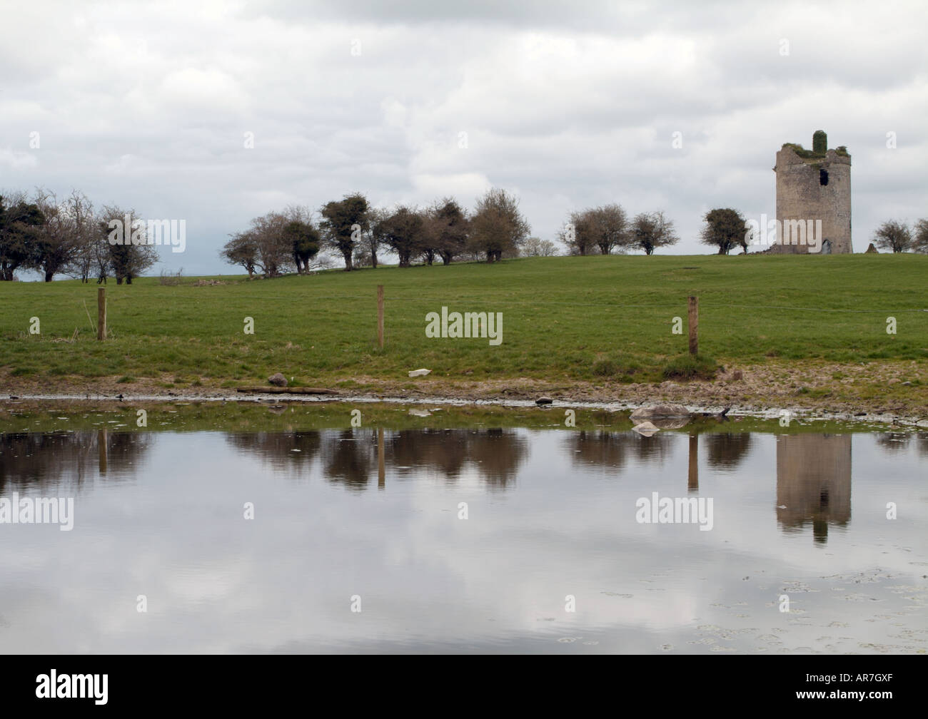 Reflection of an old norman round tower and trees in a lake on a grey ...