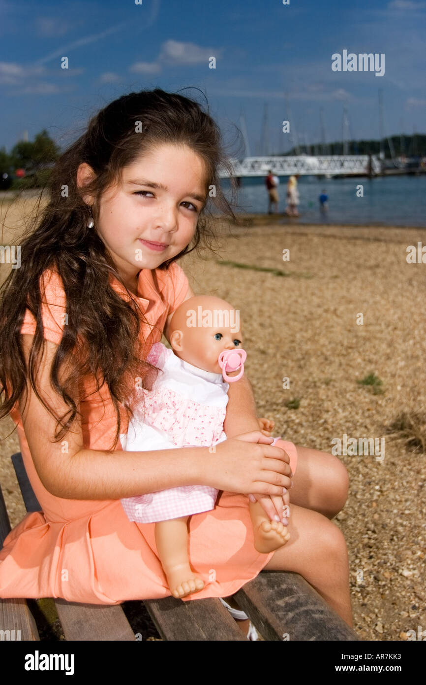 colourful portrait of young girl sitting on a bench with her doll by ...