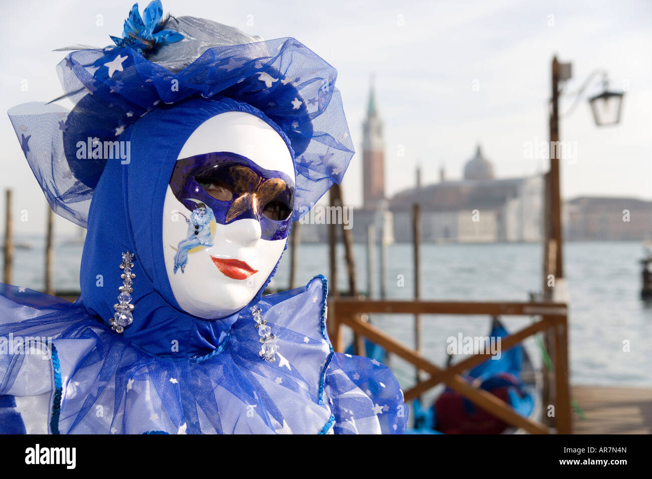 Female reveller in mask and costume by St Mark's canal with San Giorgio ...