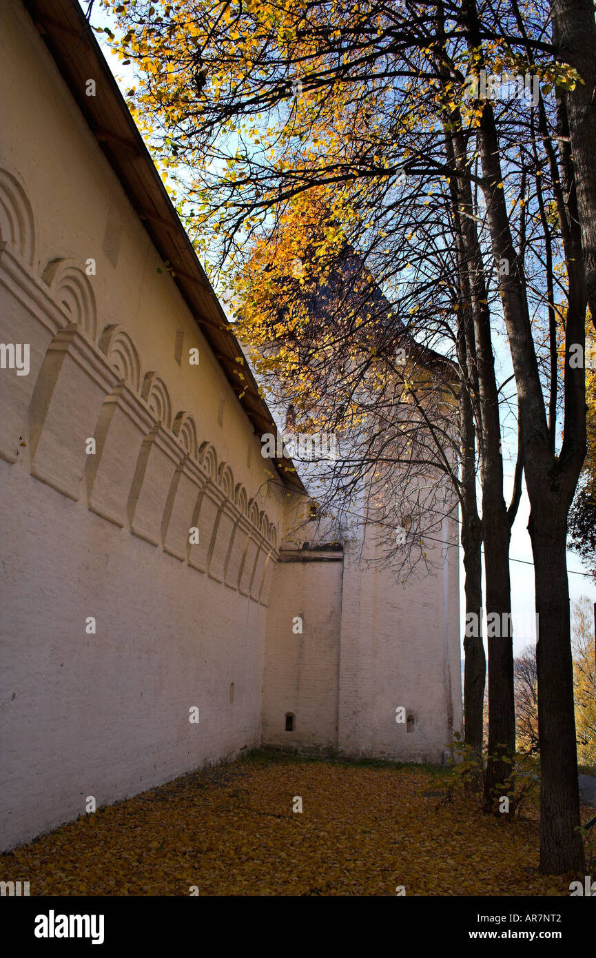a part of monastery white wall with a watchtower among autumn trees ...