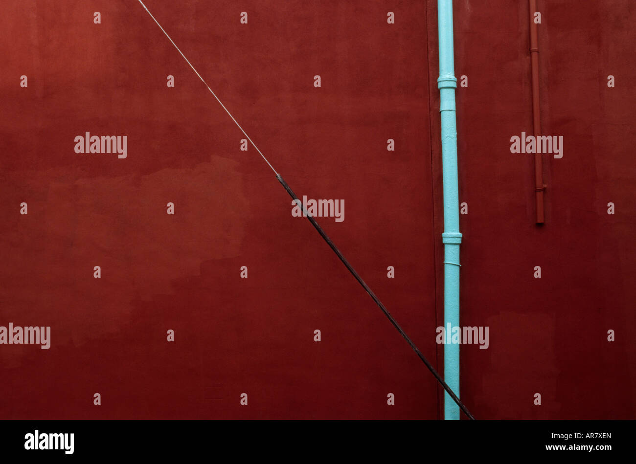 Bright rust colored wall with a aqua vertical pipe lending a strong ...