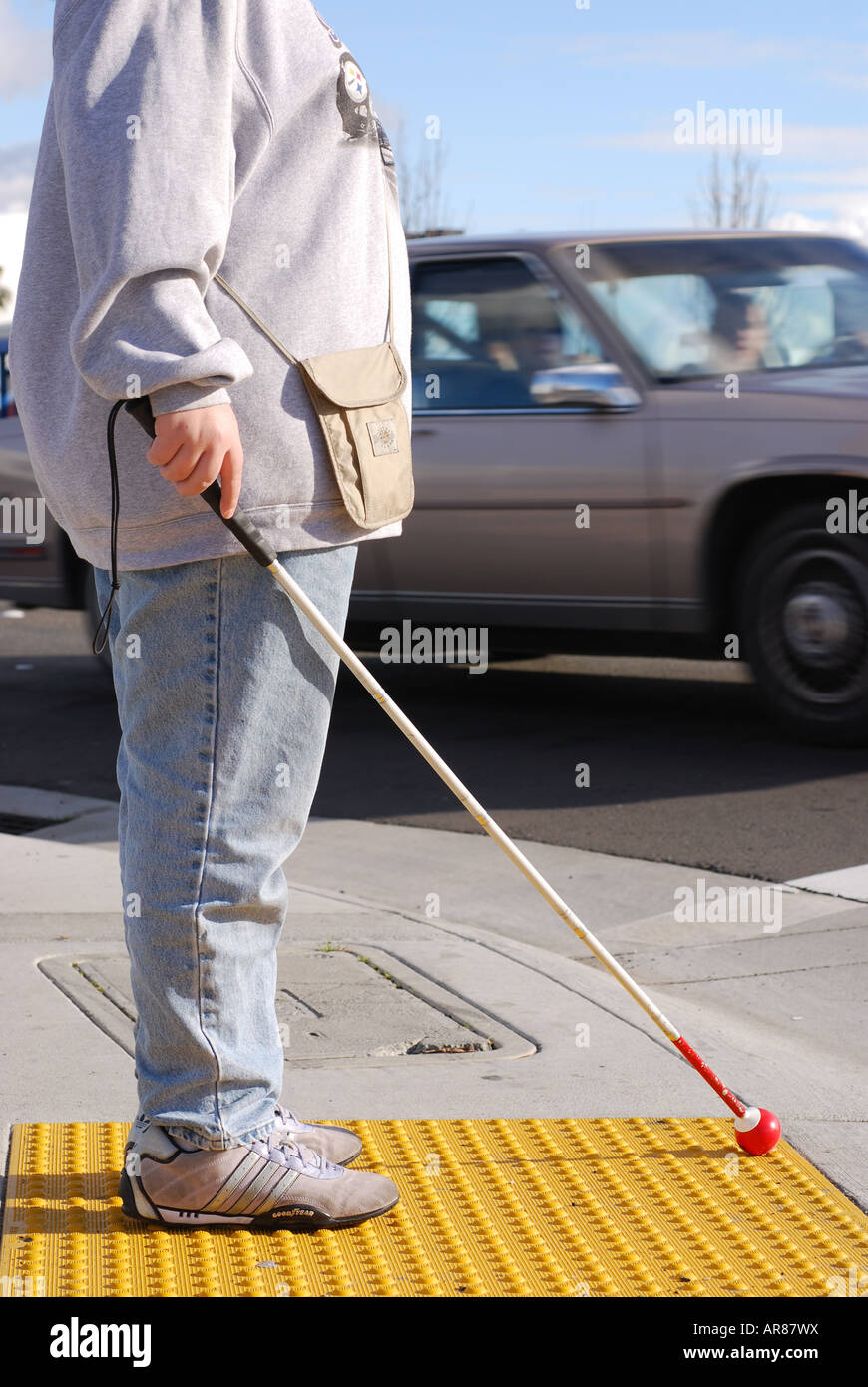 Blind woman standing on a crosswalk platform as traffic speeds past ...