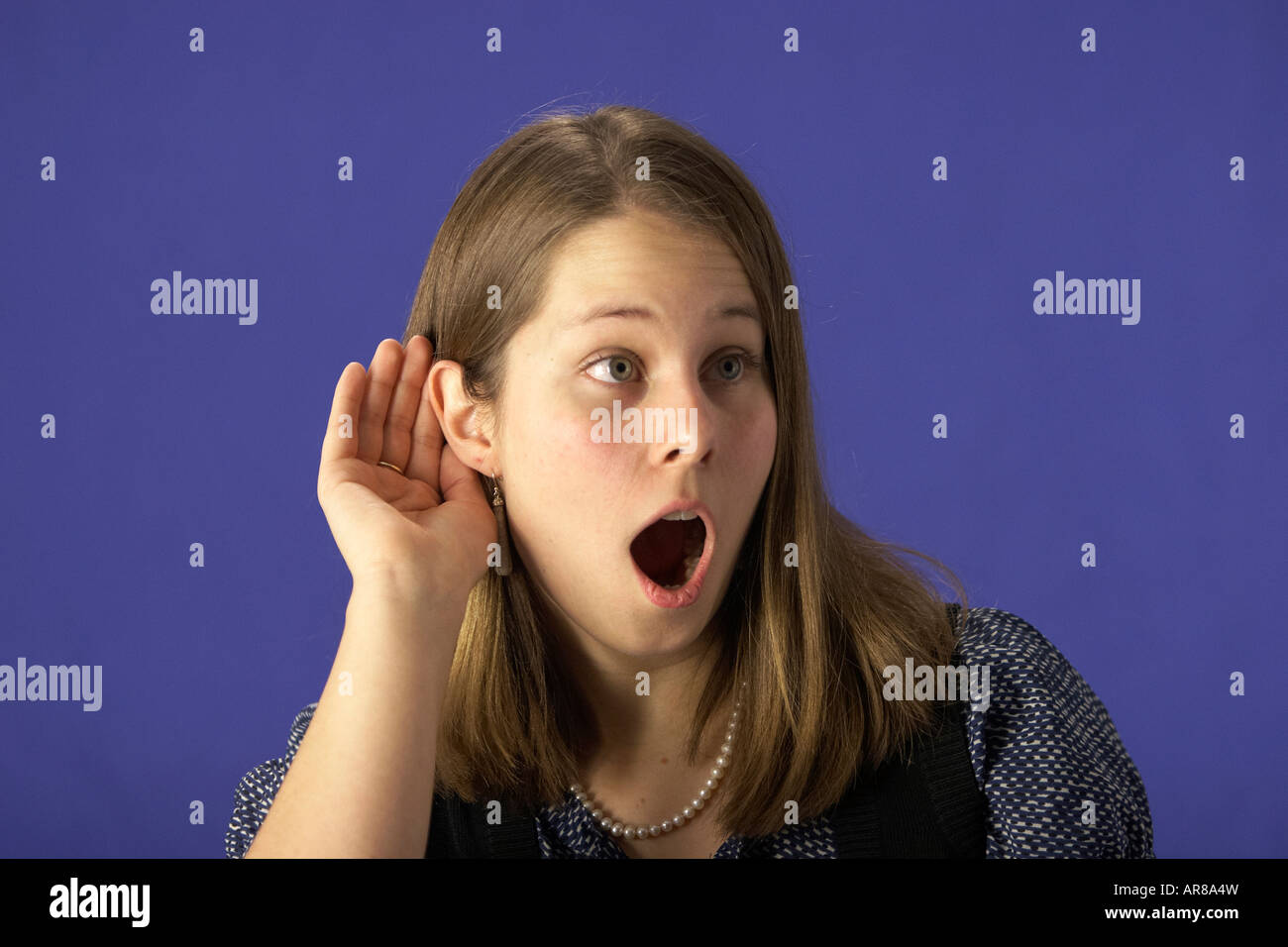 A young woman listening with hand to ear being surprised and excited ...