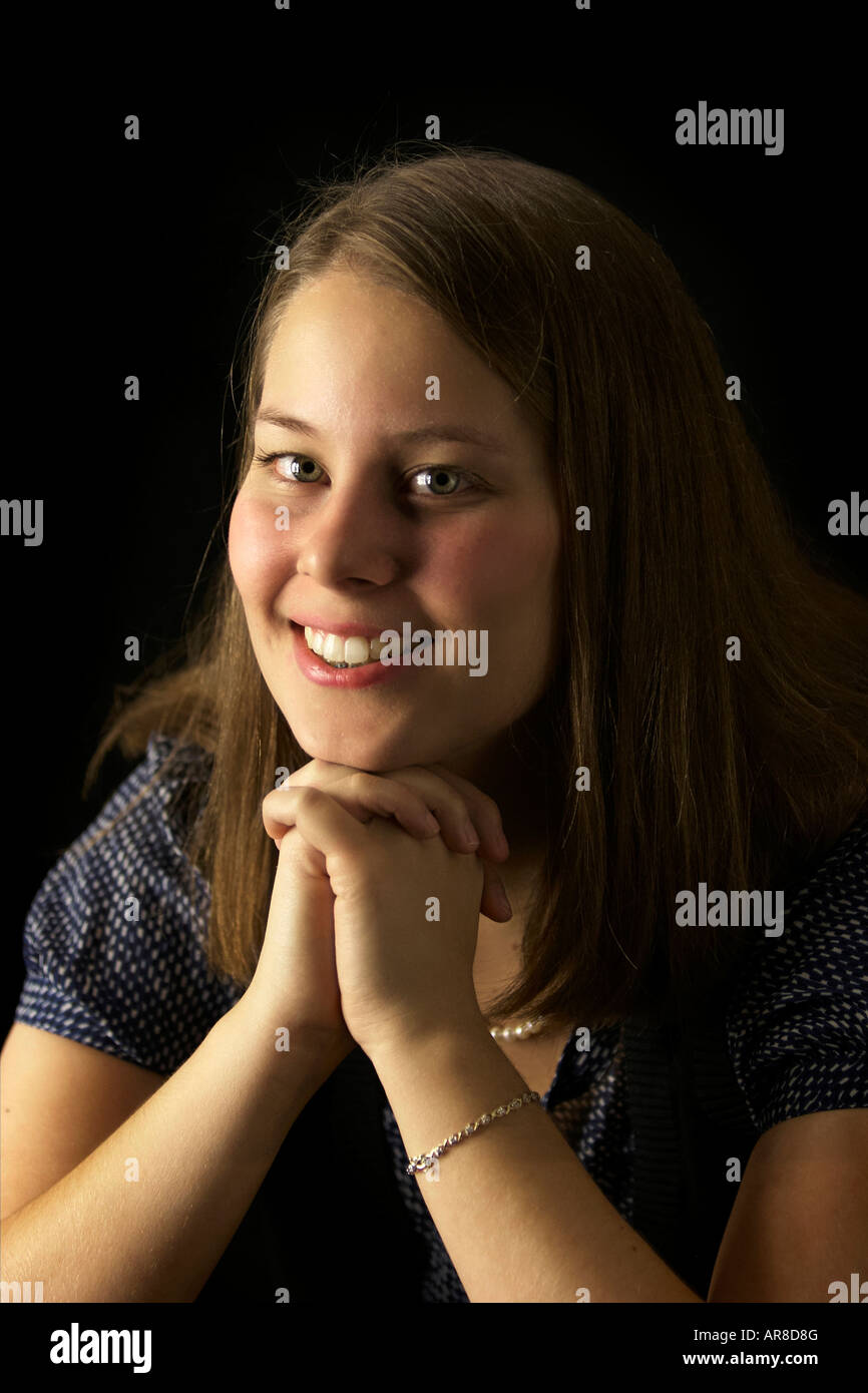 A young woman with hands resting atop her hands and smiling Stock Photo ...
