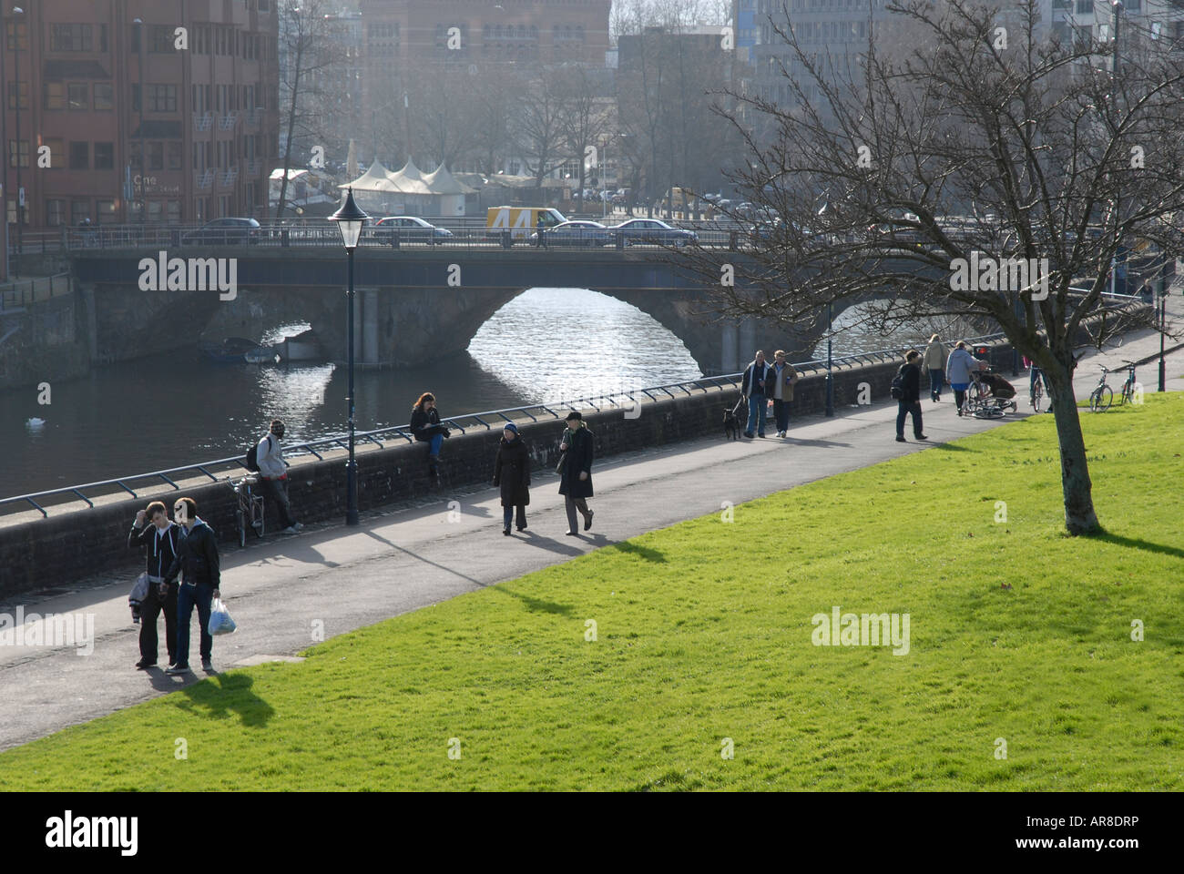 Pedestrians walking along a riverside promenade alongside Castle Park ...