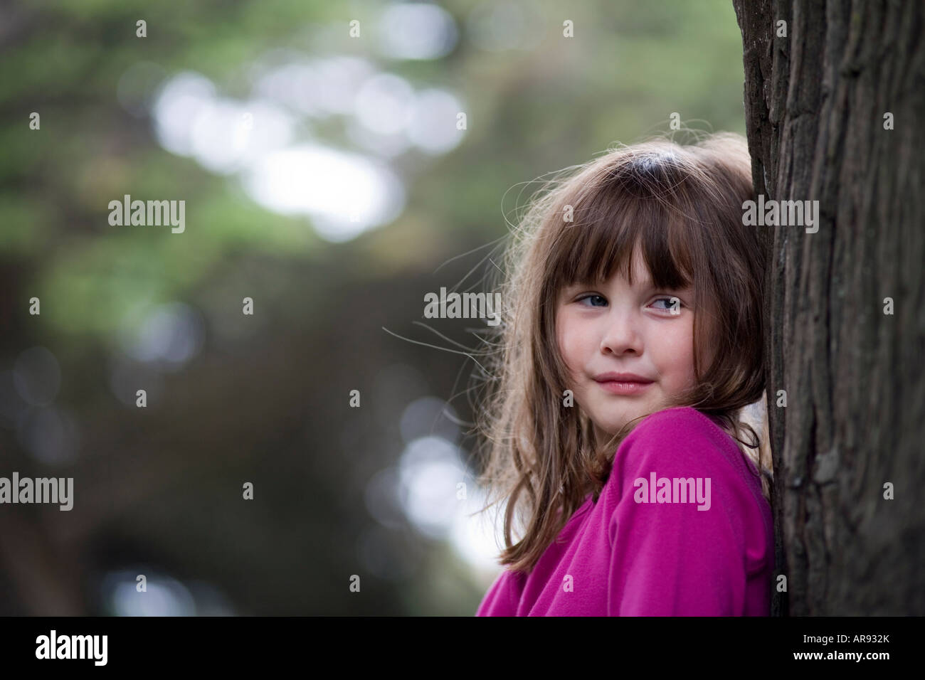 Young girl leaning against tree looking into the distance Stock Photo ...