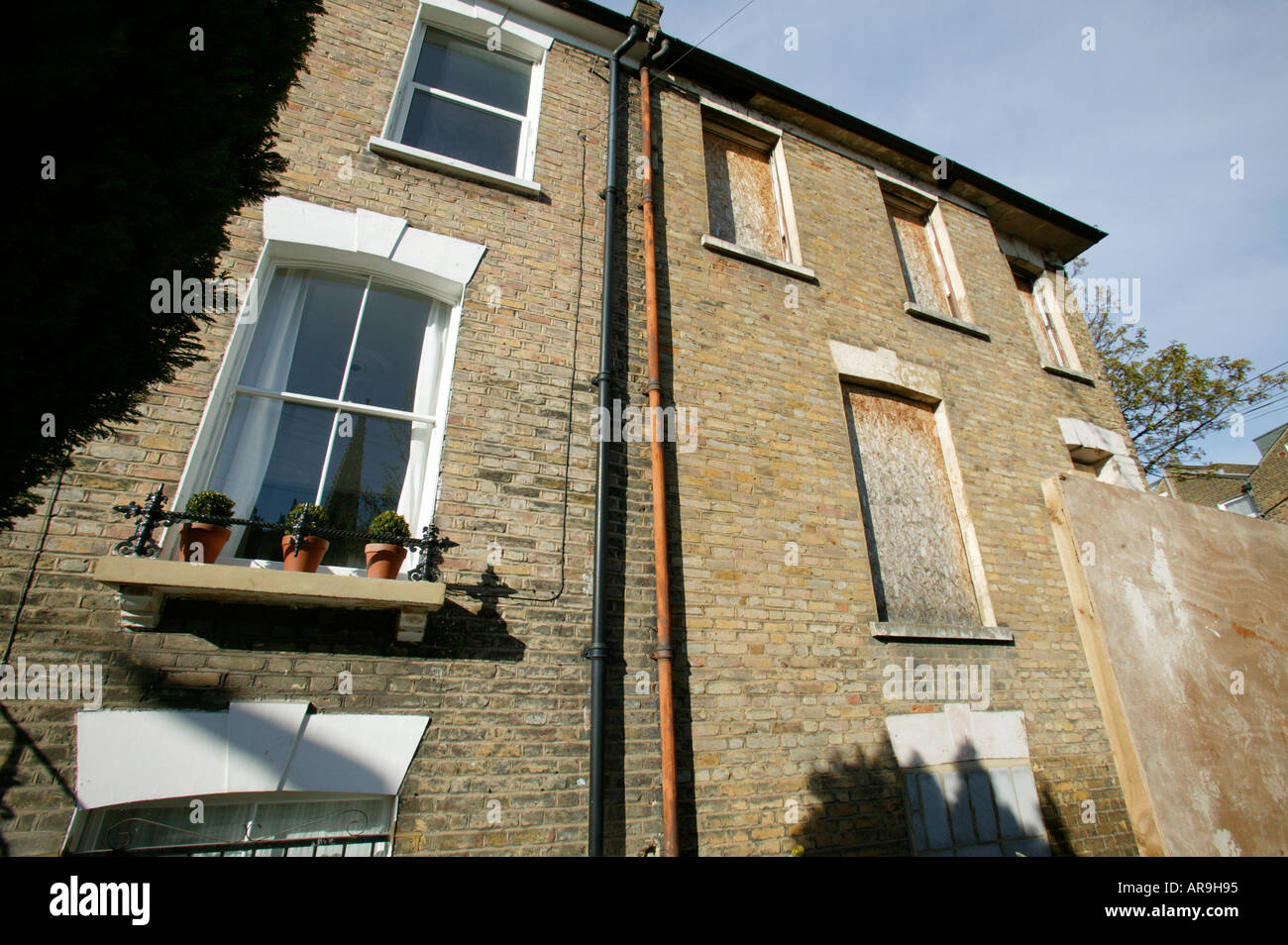 derelict boarded up house next to well tended house Stock Photo - Alamy