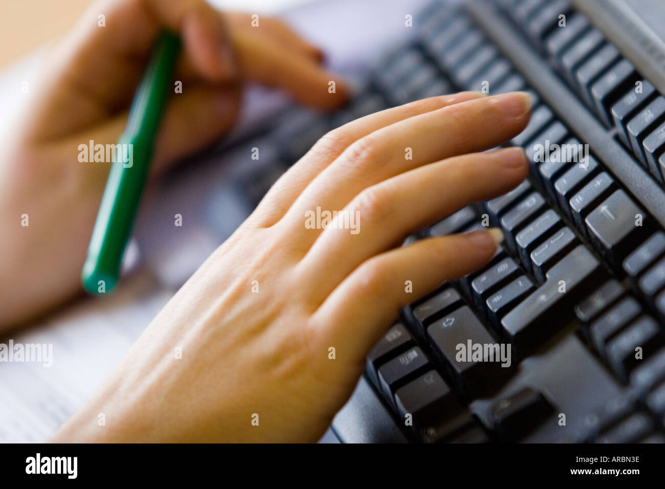 Female typing on keyboard, pen in hand Stock Photo - Alamy