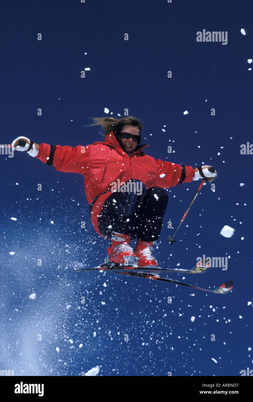 Female skier flying through the air with flakes of snow all around her ...