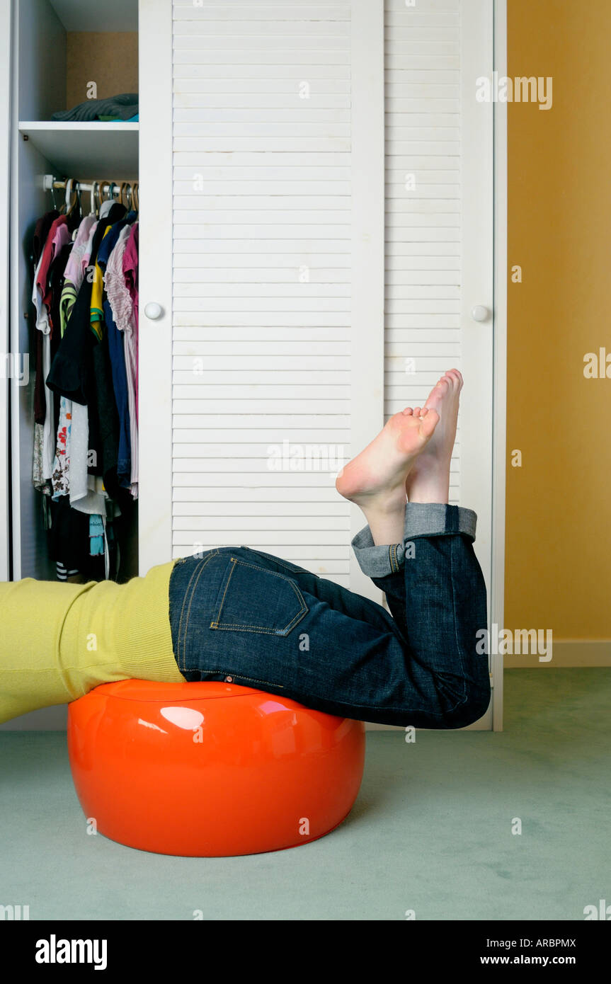 Person relaxing on an orange stool in a room with a closet full of ...