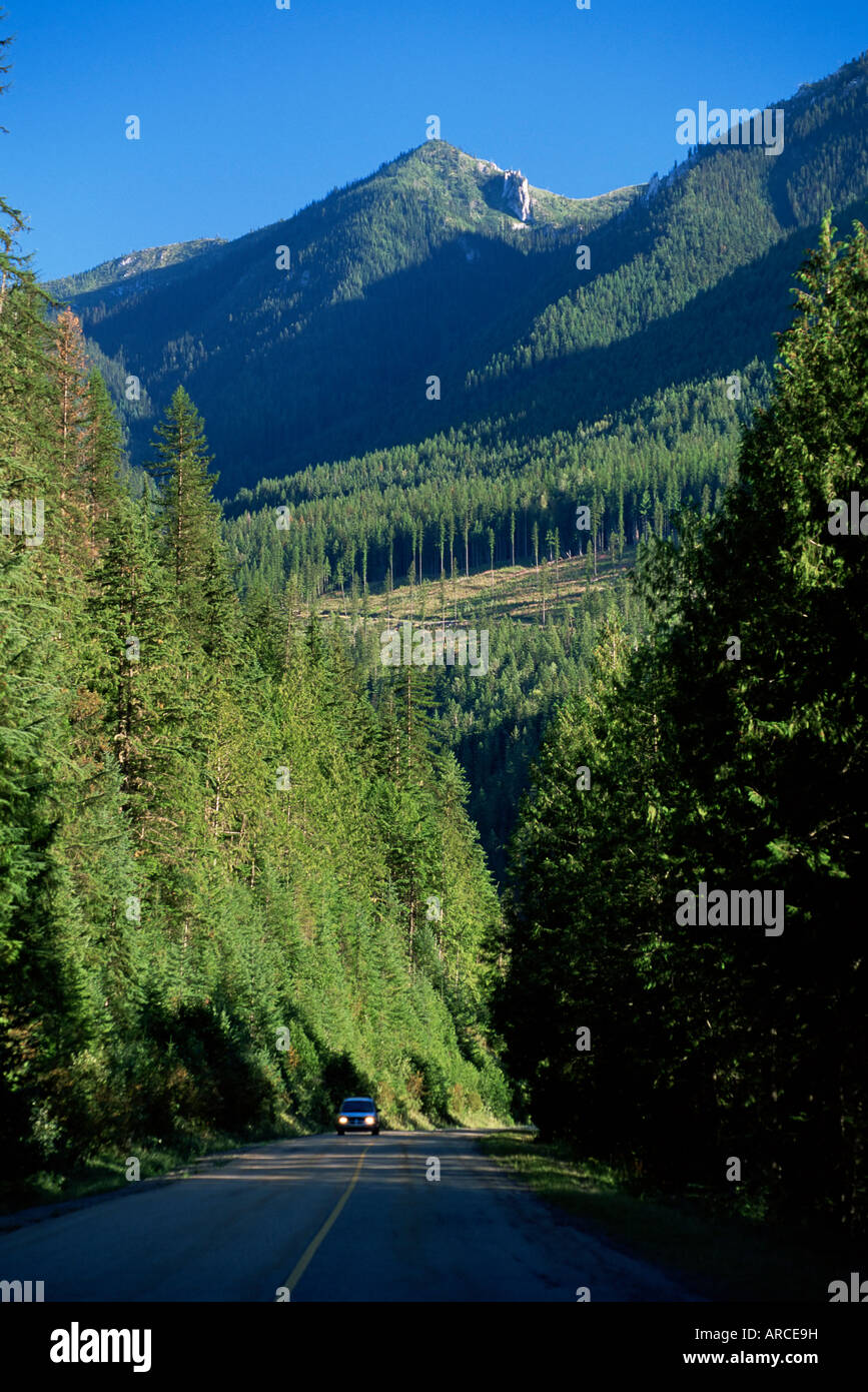Car on Route 31A dwarfed by steep tree-covered slopes, near Kaslo ...