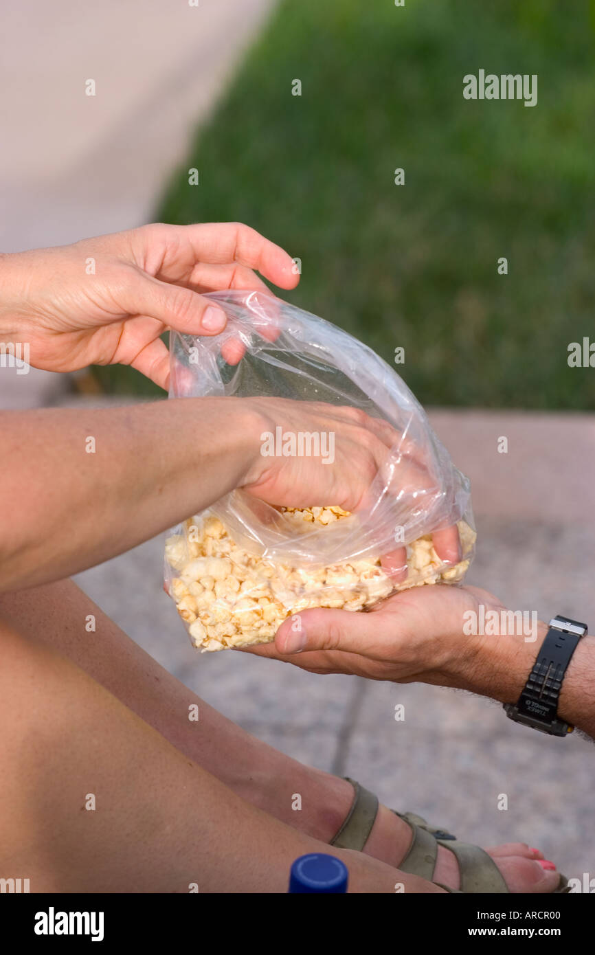 Man s hand offering popcorn from a plastic bag to another set of hands ...