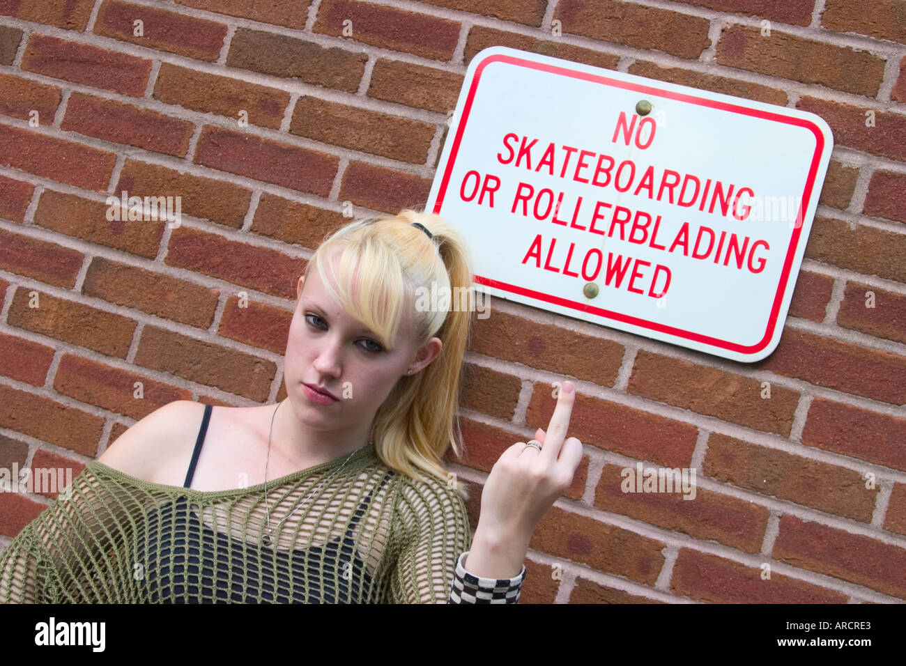 Teen girl giving the finger to a sign reading NO SKATEBOARDING OR ...