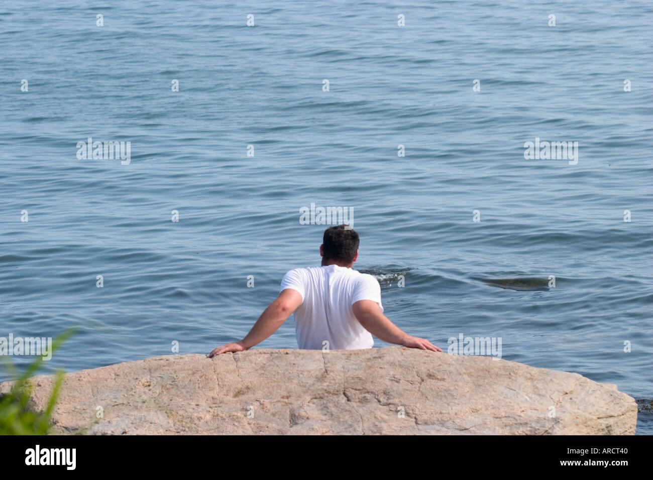 Man sitting on a rock at the beach looking into the water Stock Photo ...