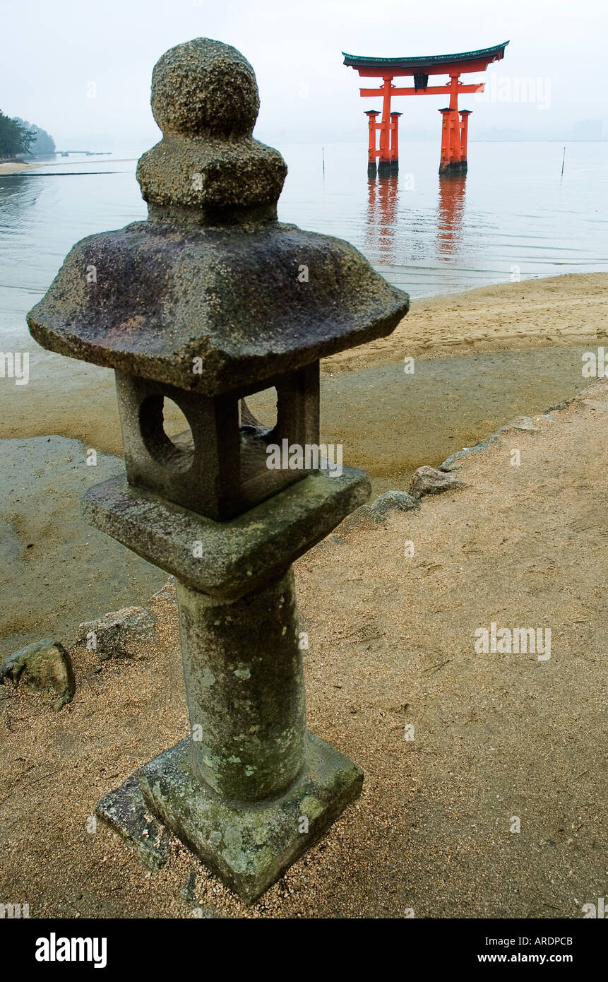 A stone lantern stands in front of the floating torii gate of Miyajima ...