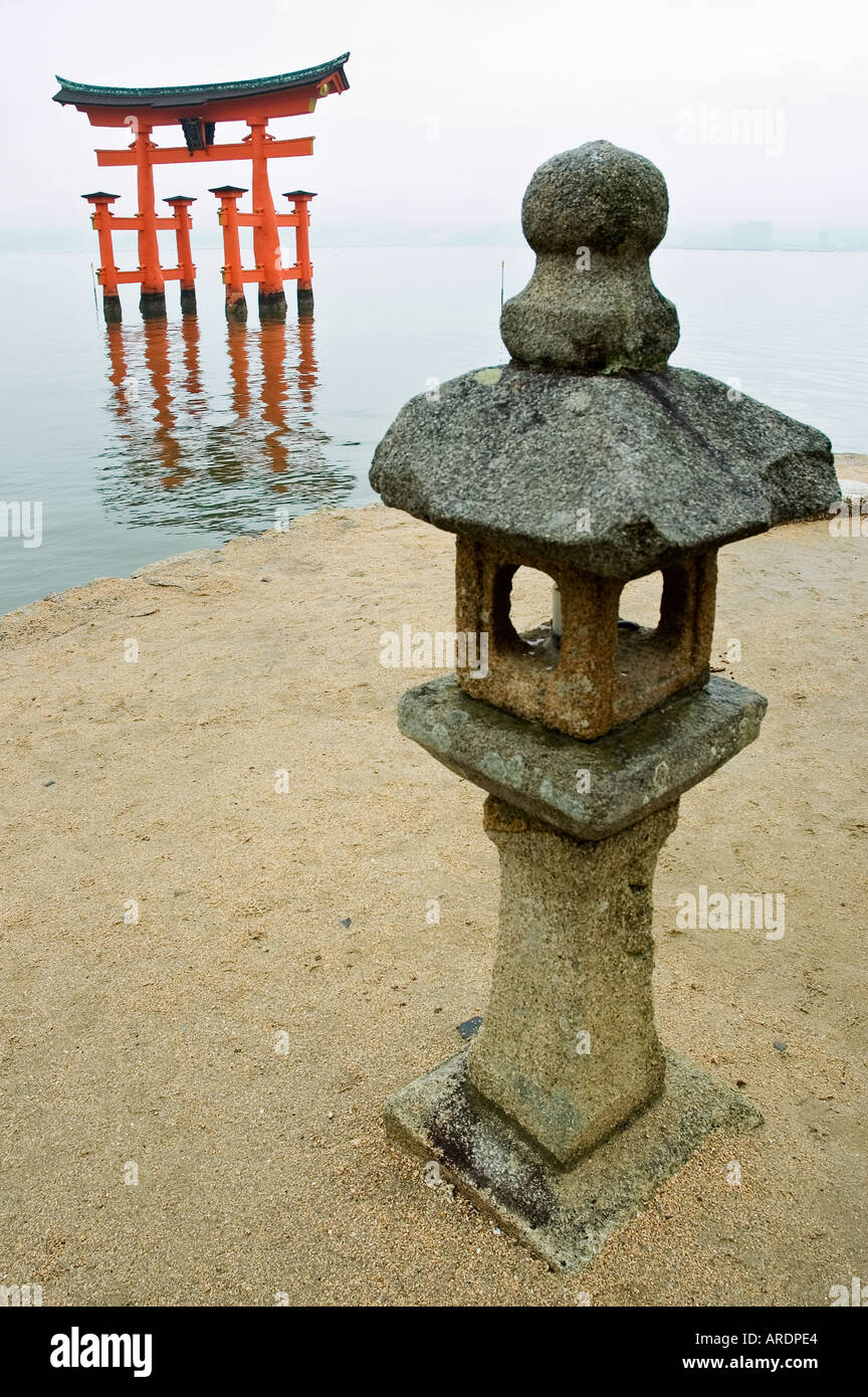 A stone lantern stands in front of the floating torii gate of Miyajima ...