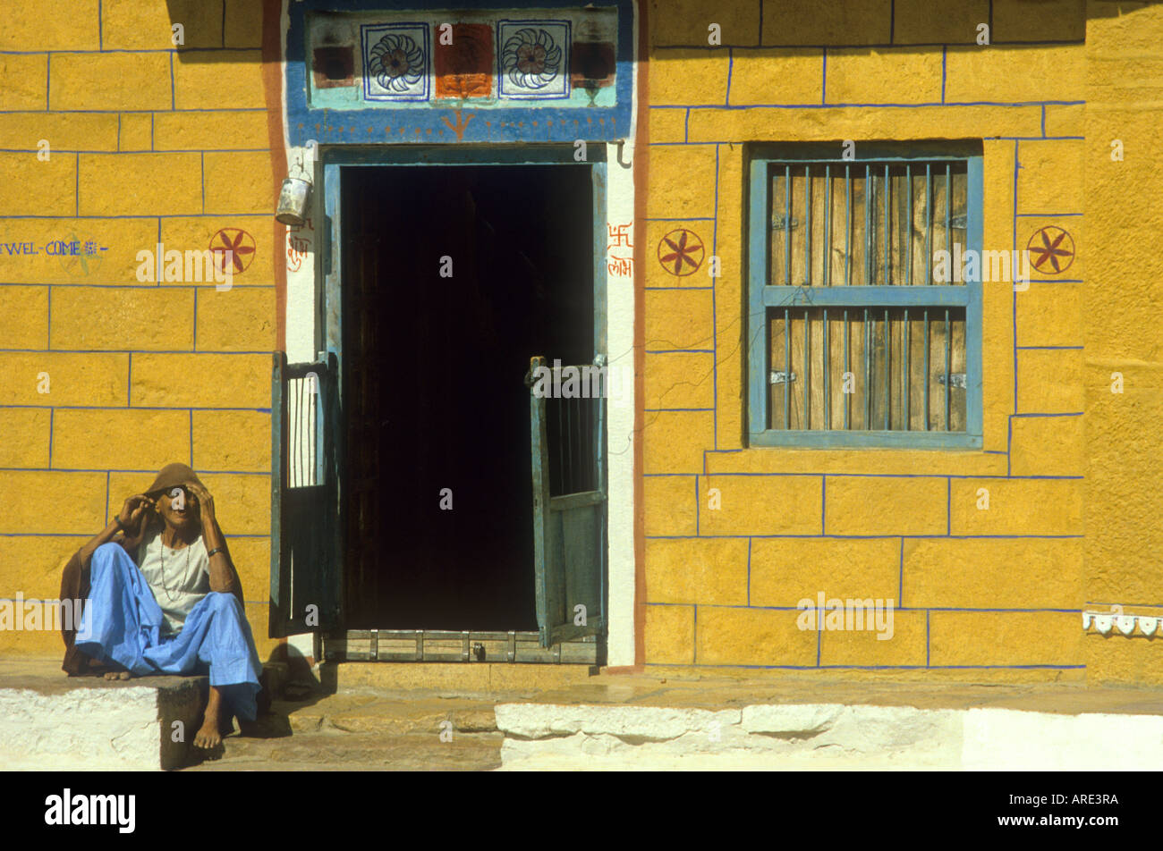 Local woman sits in the sun outside her brightly painted house near the ...