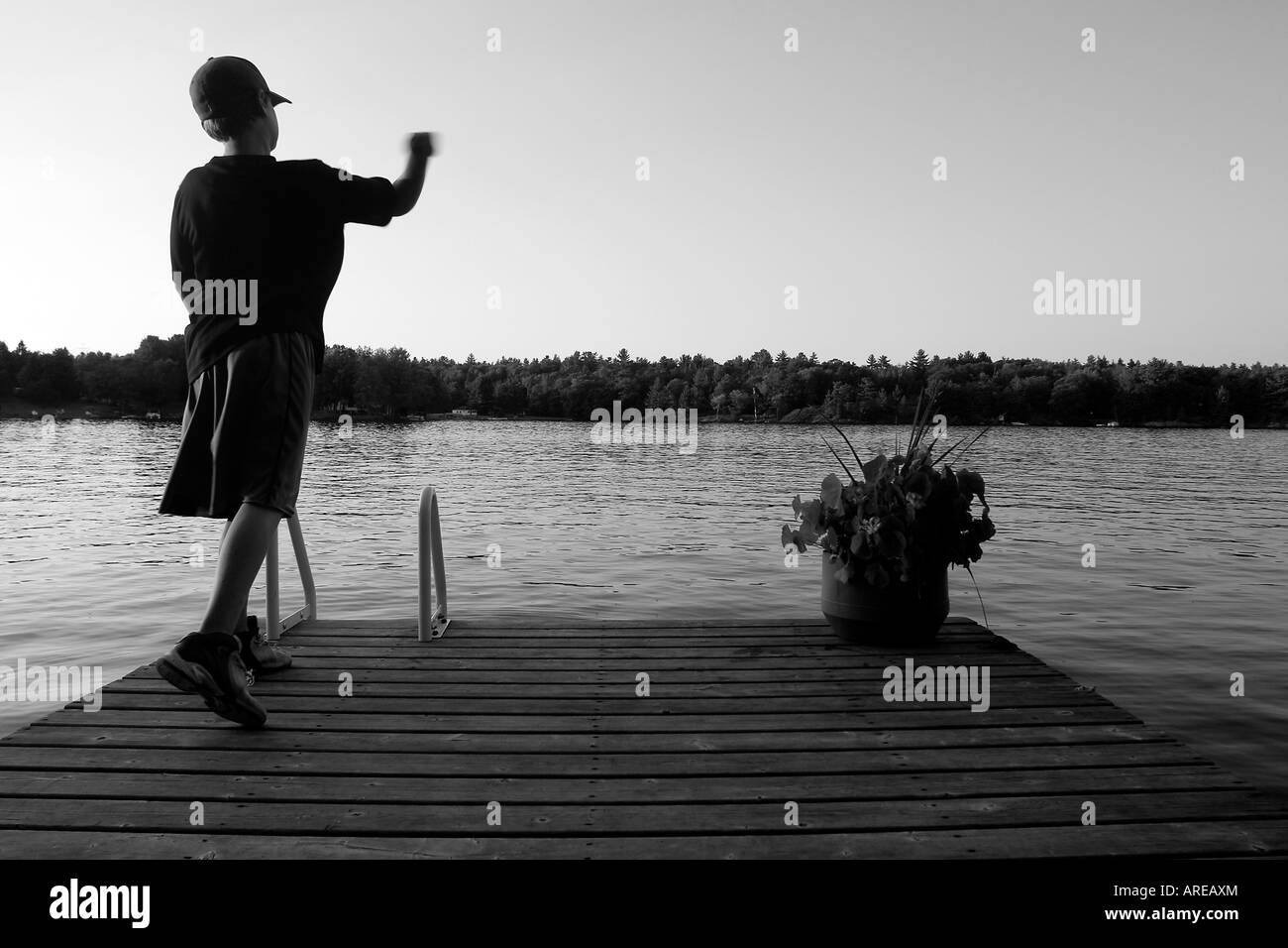 Boy on dock on lake throwing Stock Photo - Alamy