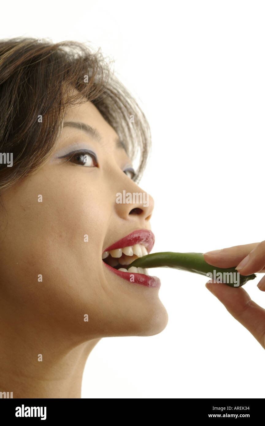 headshot of attractive female with red lips holding hot green chilli ...