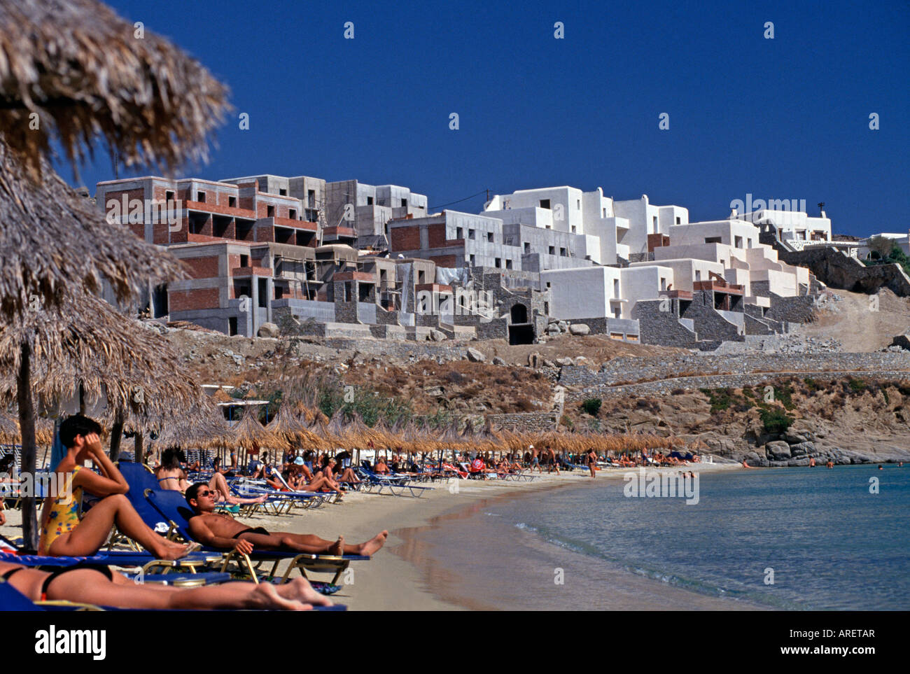 Sunbathers and new construction along shoreline Psarou Beach Mykonos Greece Stock Photo - Alamy