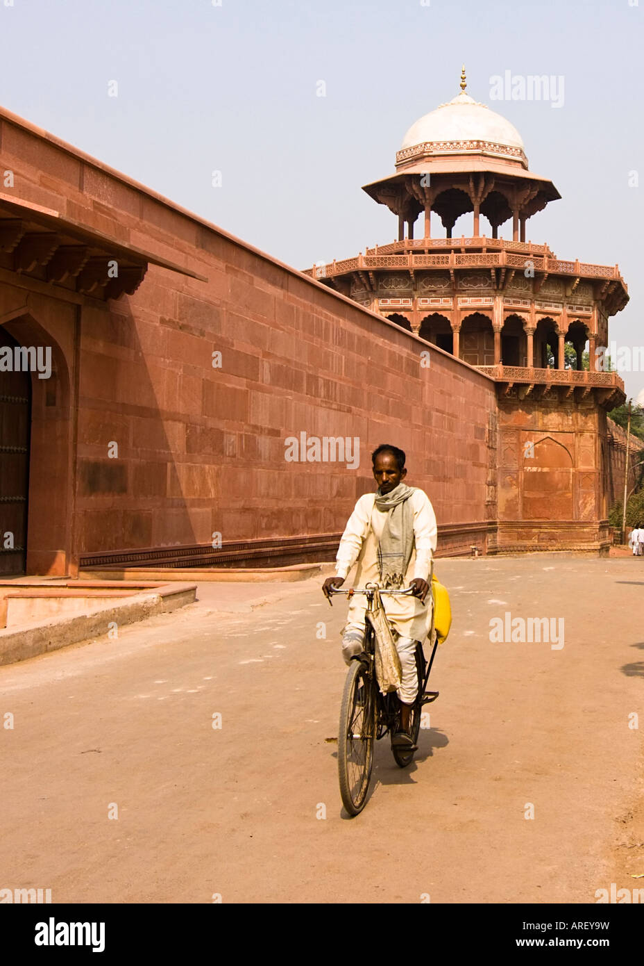 An indian man riding his bicycle near the red sandstone wall ...