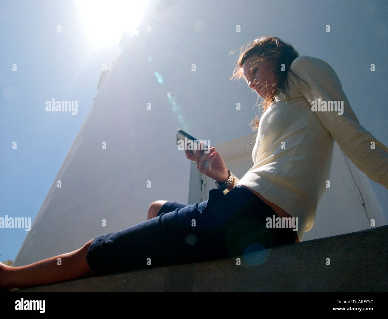 a low angle shot of young woman sitting on wall reading her texts and e ...