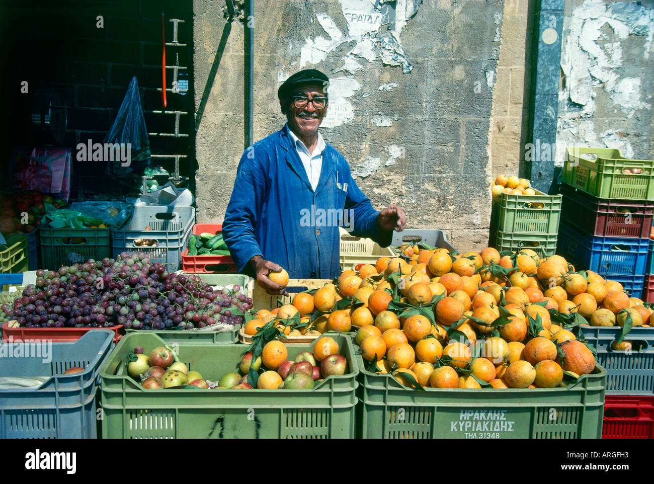 A smiling trader standing behind his stall on which are displayed piles ...