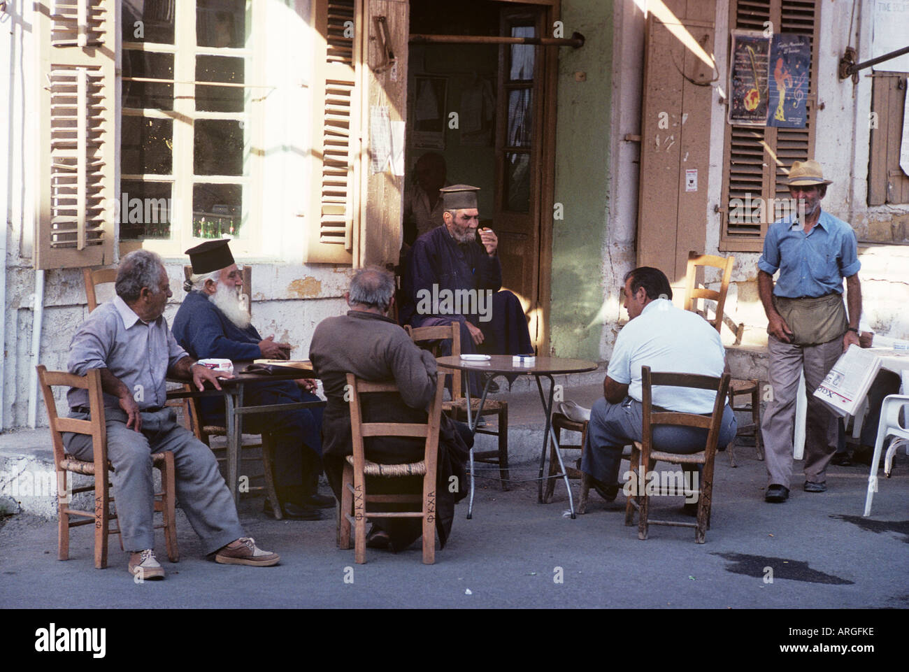 Bearded priests in their black robes chat to villagers at tables ...