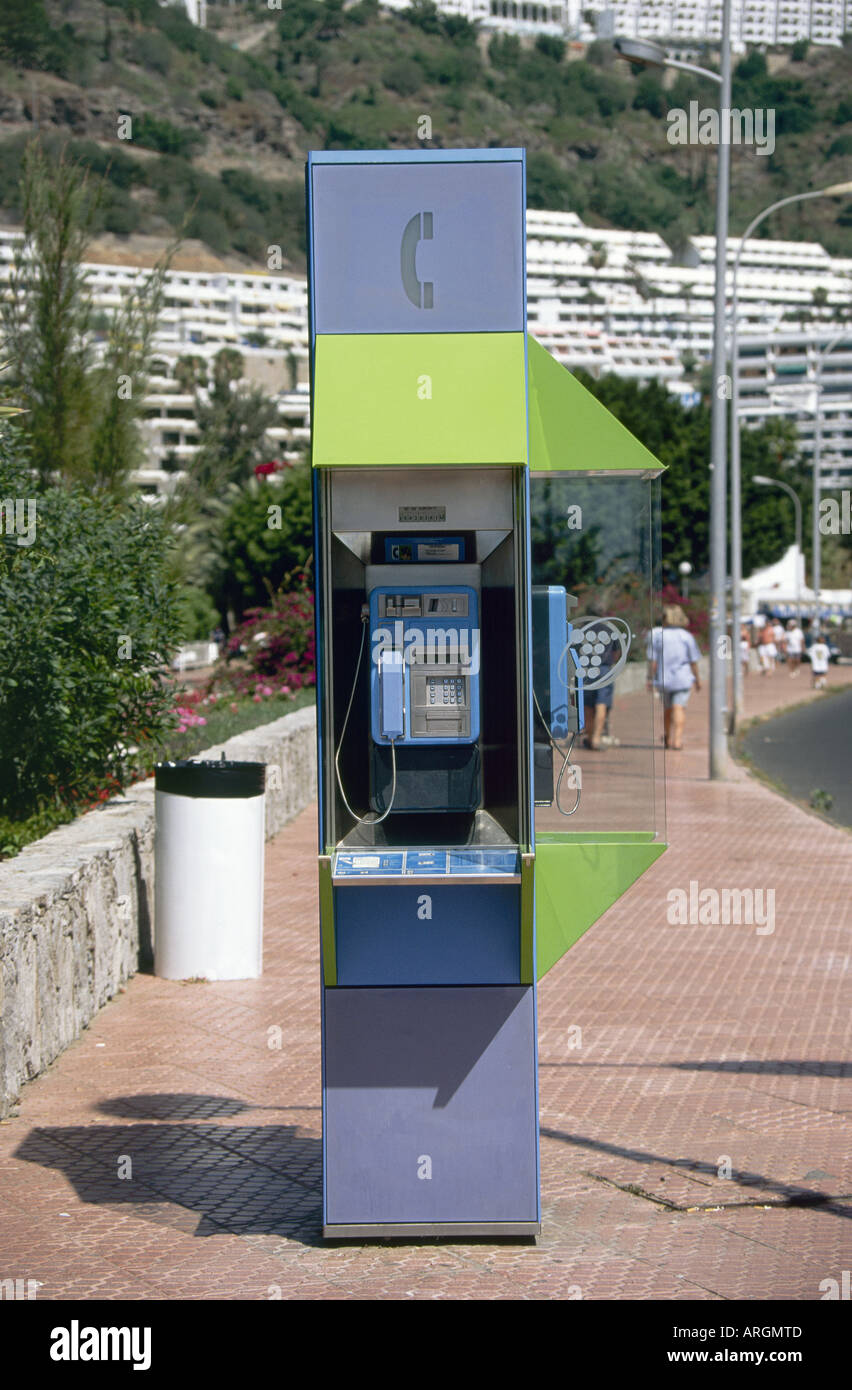 A green and blue public telephone booth on a paved sidewalk of a resort ...