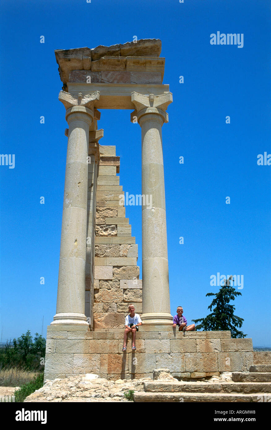 A couple of children sitting on the base of the remains of a colonnade ...