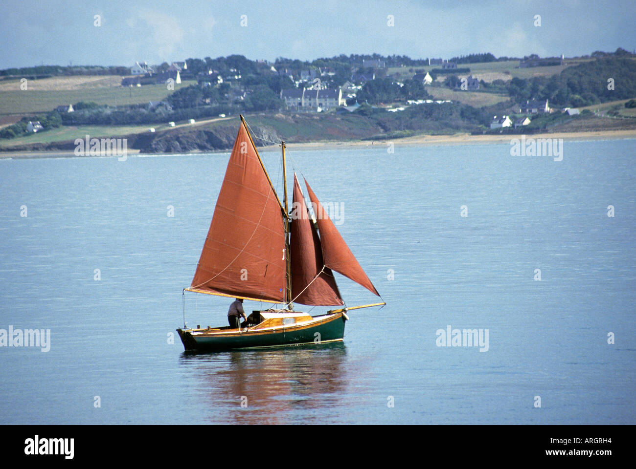 Dark red sails set an old gaff rigged sailing boat approaching a ...