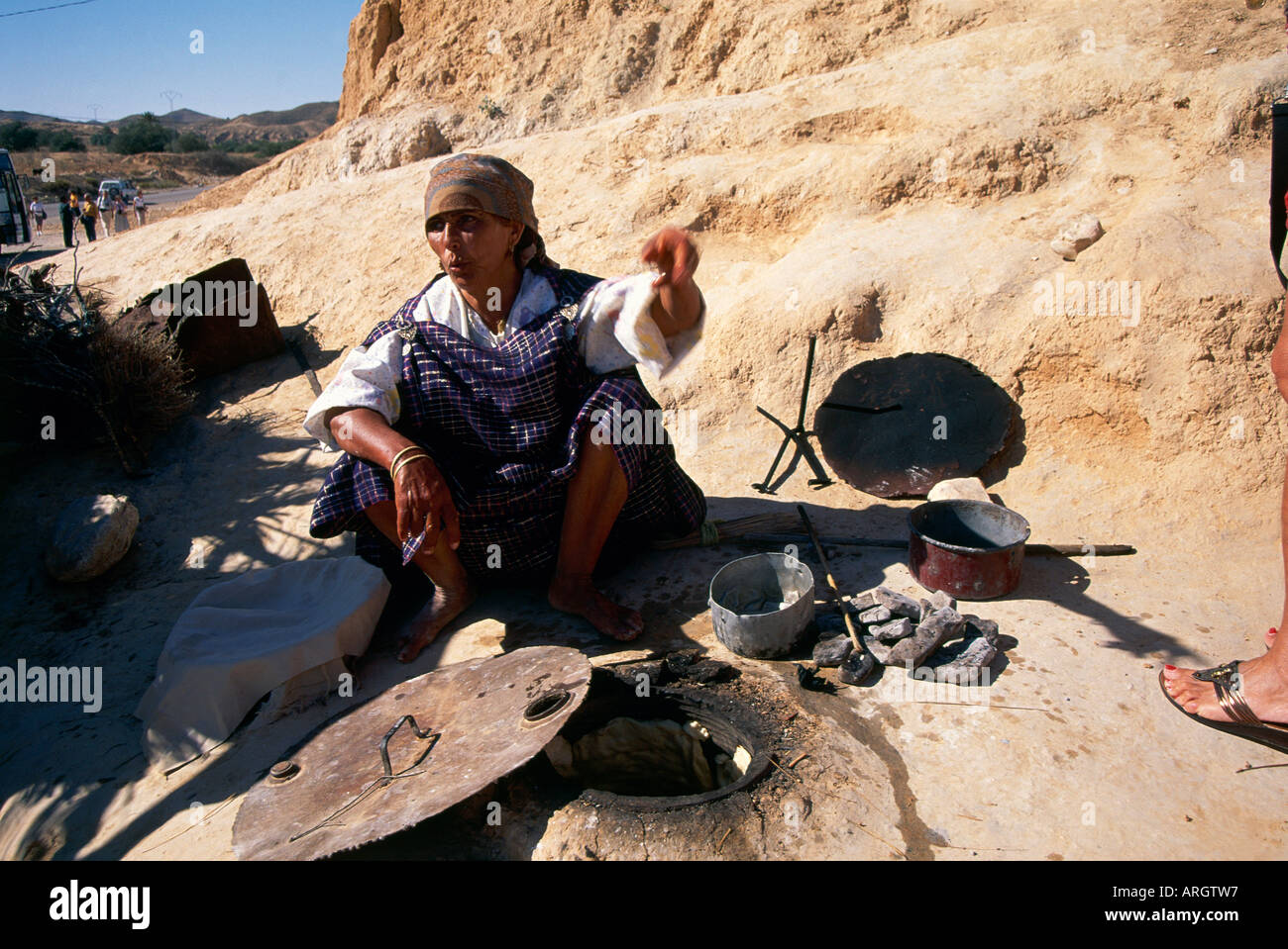 A dark skinned Berber woman baking bread on an open stove in one of one ...