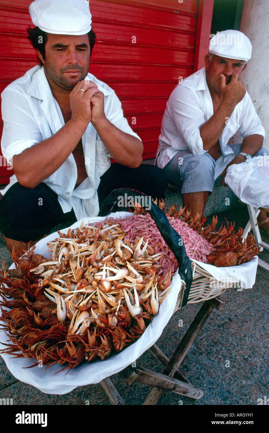 Vendors of seafood wearing white shirts and caps sit beside their wares ...