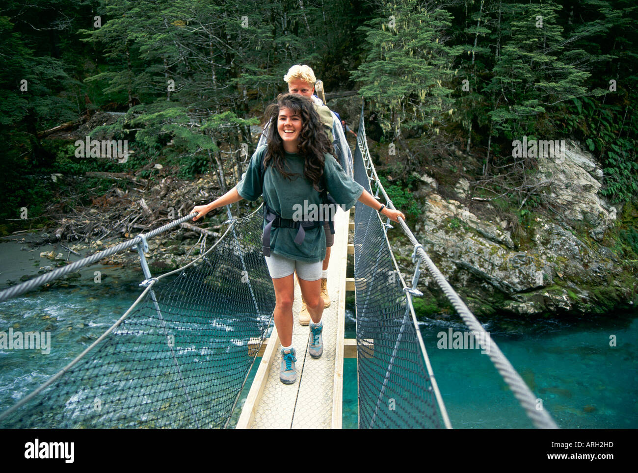With loaded packs hikers cross a narrow bridge over a river gorge on ...
