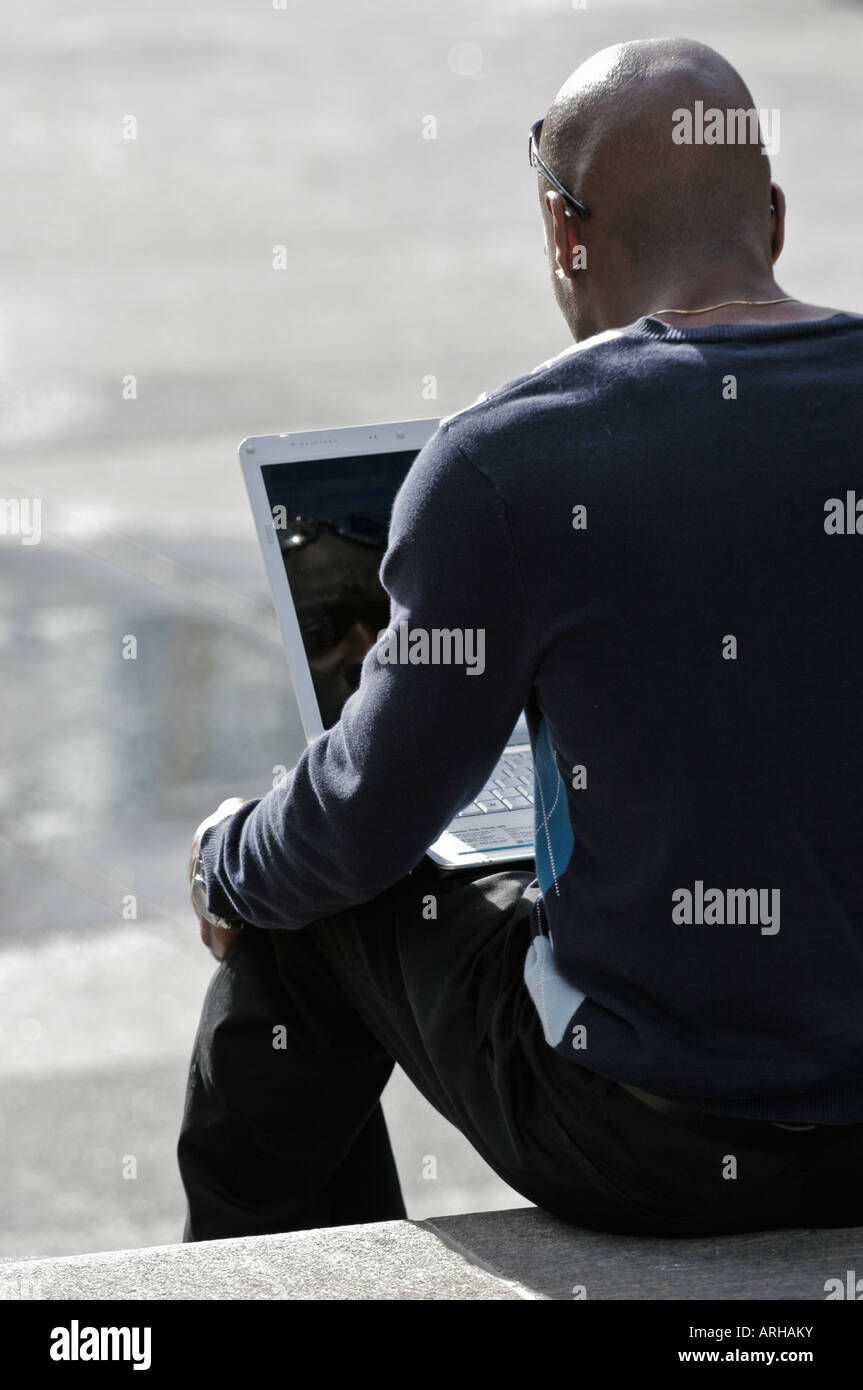 Backlit rear view of a bald coloured man in grey seated in the street ...