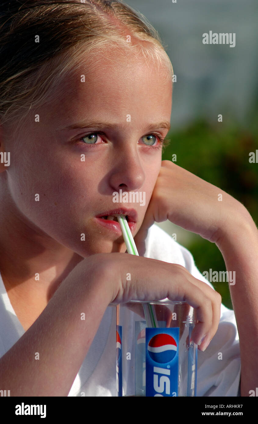 Sad young girl drinking a soft drink through a straw looking into ...