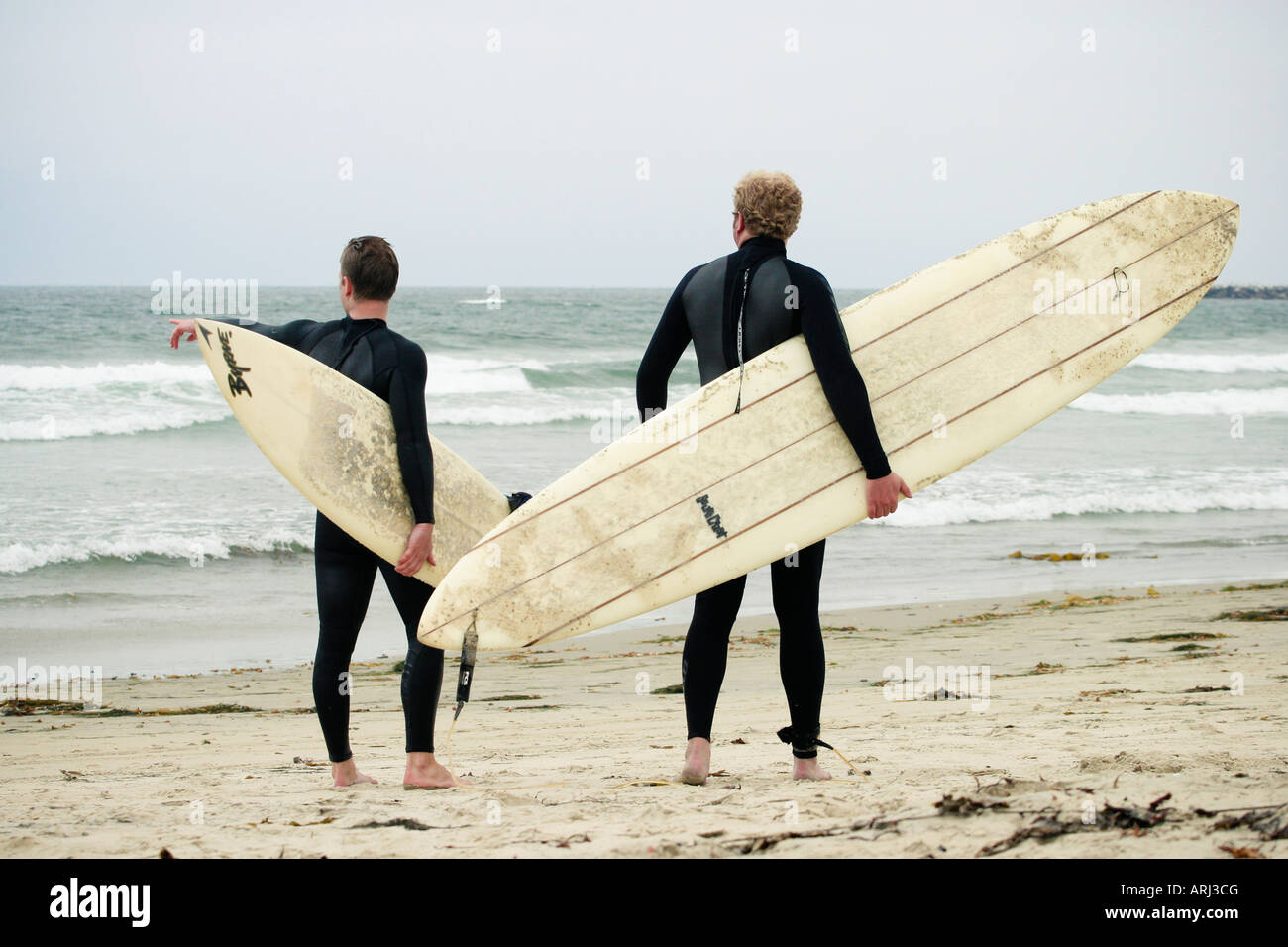 Two male surfers standing on the beach holding their surfboards Stock ...