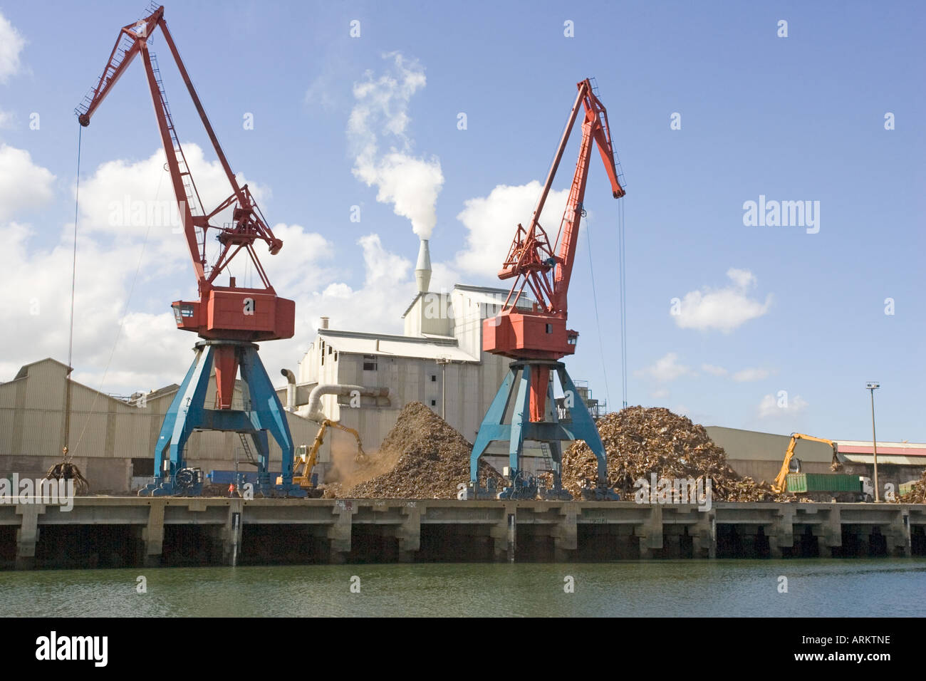 Cranes on quayside unloading scrap metal into trucks for reprocessing ...