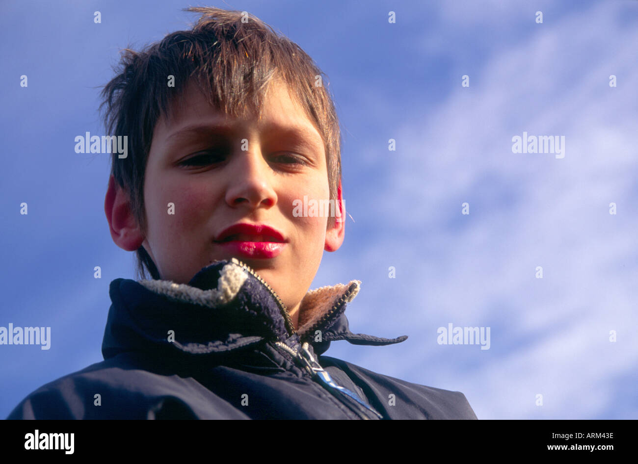Boy looking down against blue sky and clouds in background Stock Photo ...