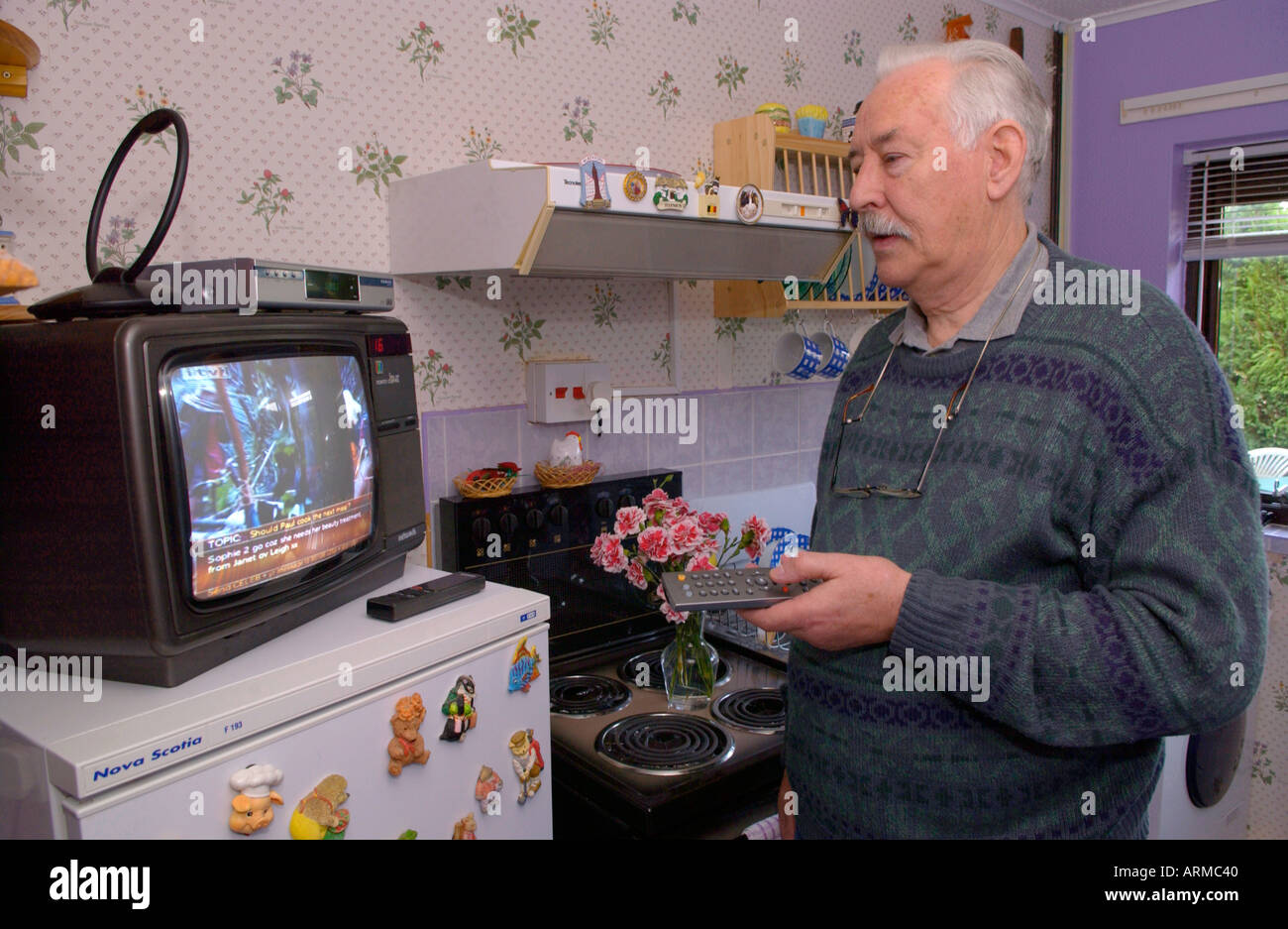 Elderly man using his television digital set top box in kitchen of home ...