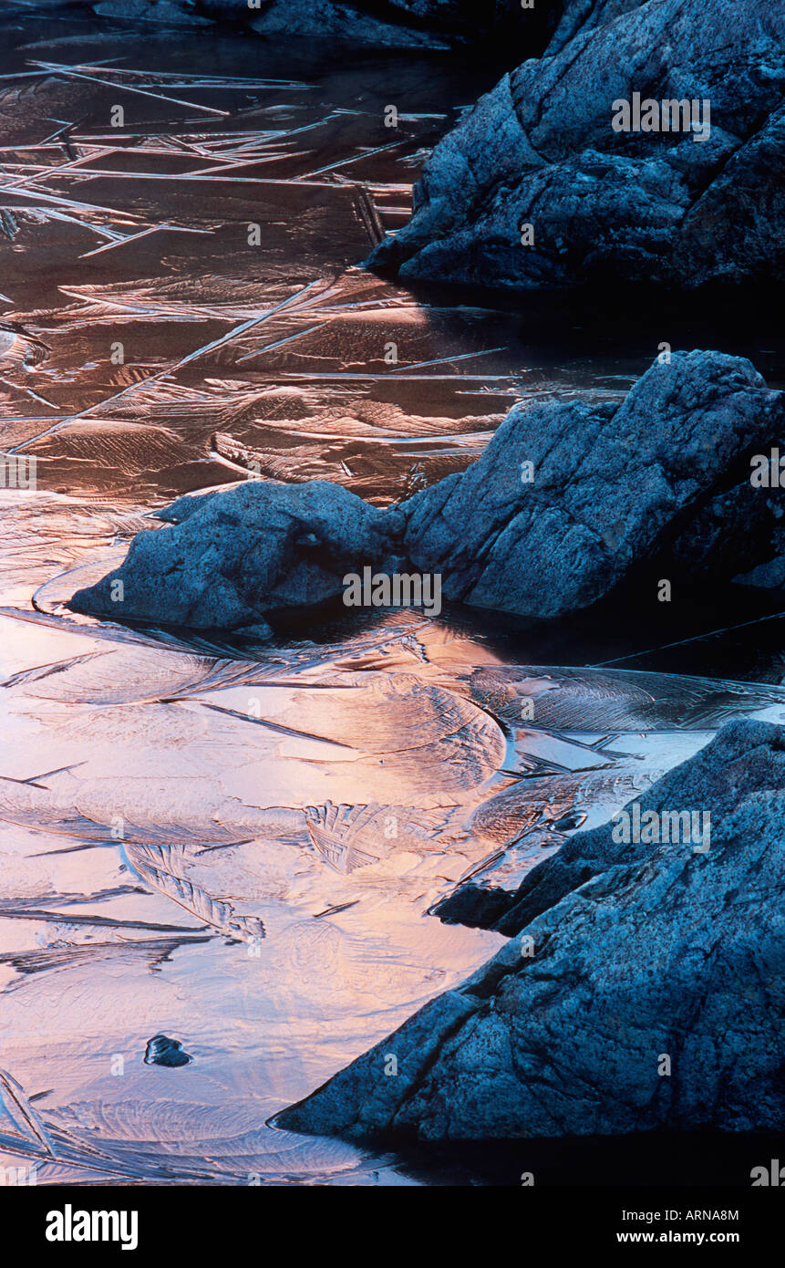 Frozen pond patterns reflecting warm sky with granite boulders, British ...
