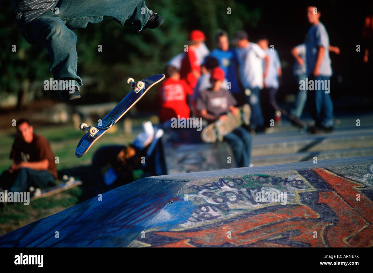 Skateboarder kickflips board over pyramid in graffiti painted skatepark ...
