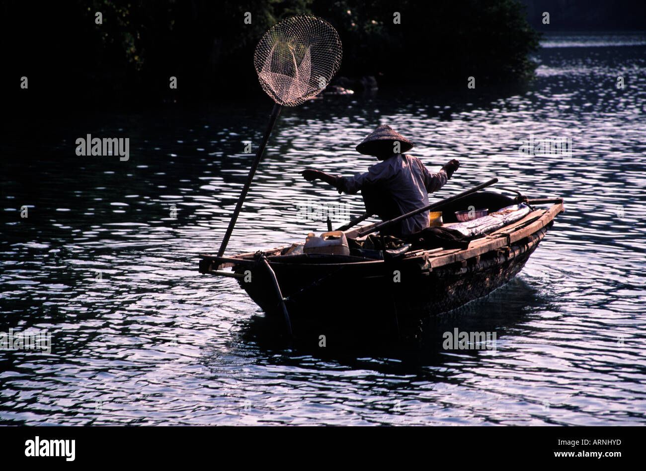 Fisherman wearing traditional conical straw hat in wooden boat with net ...
