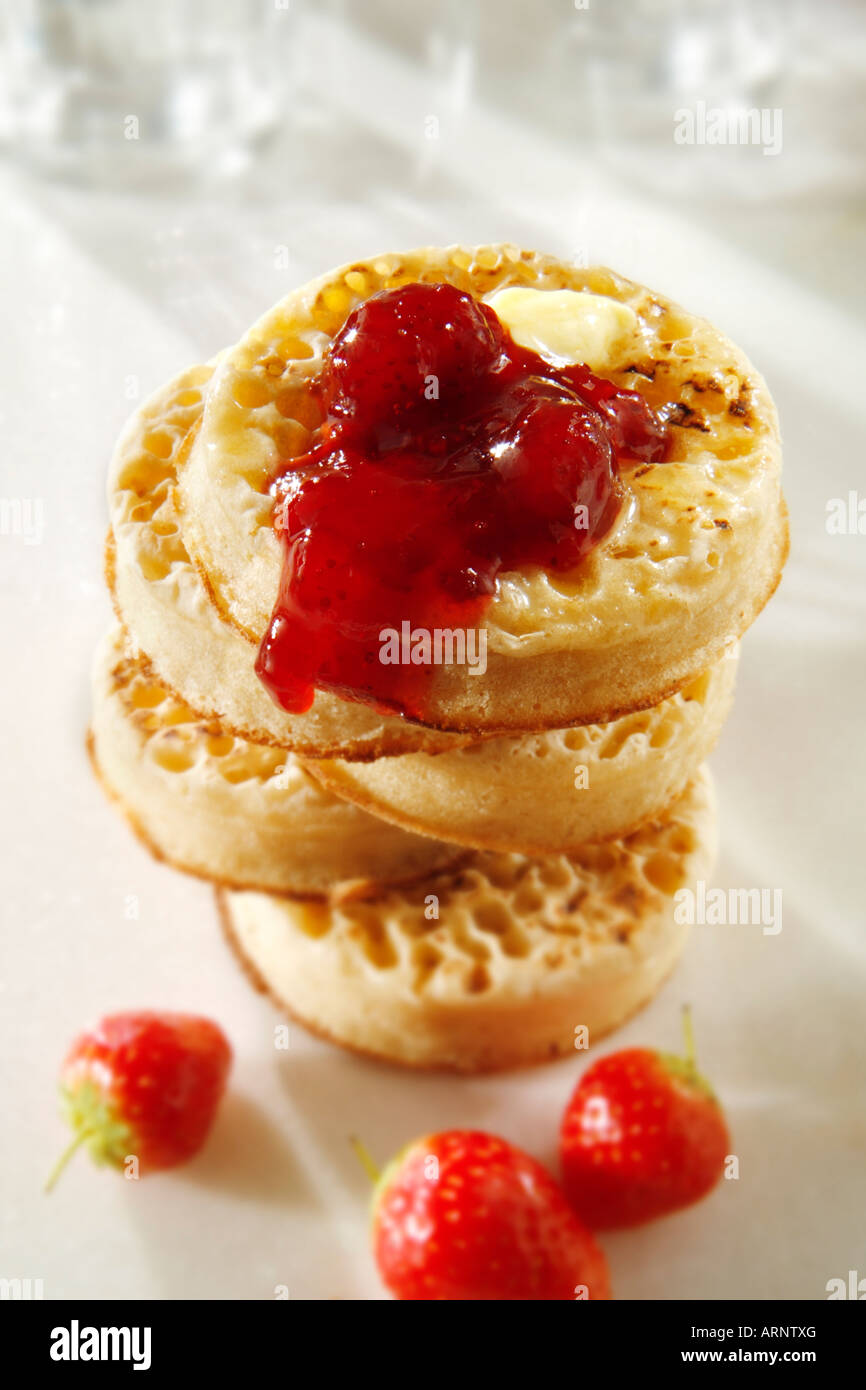 Close up of buttered toasted crumpets with strawberry jam ready to eat ...