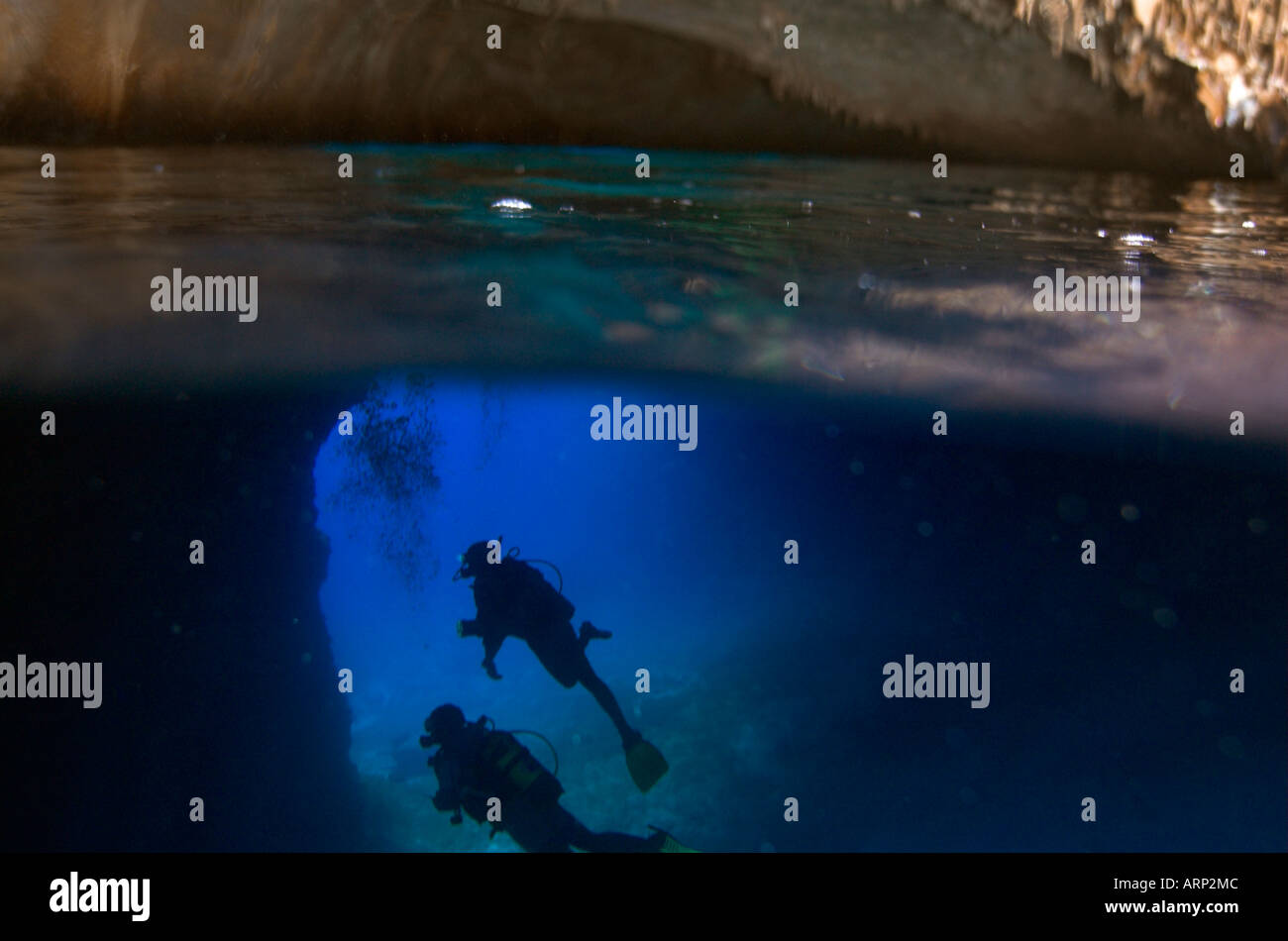 Divers in sea cave silhouetted against blue of underwater entrance ...