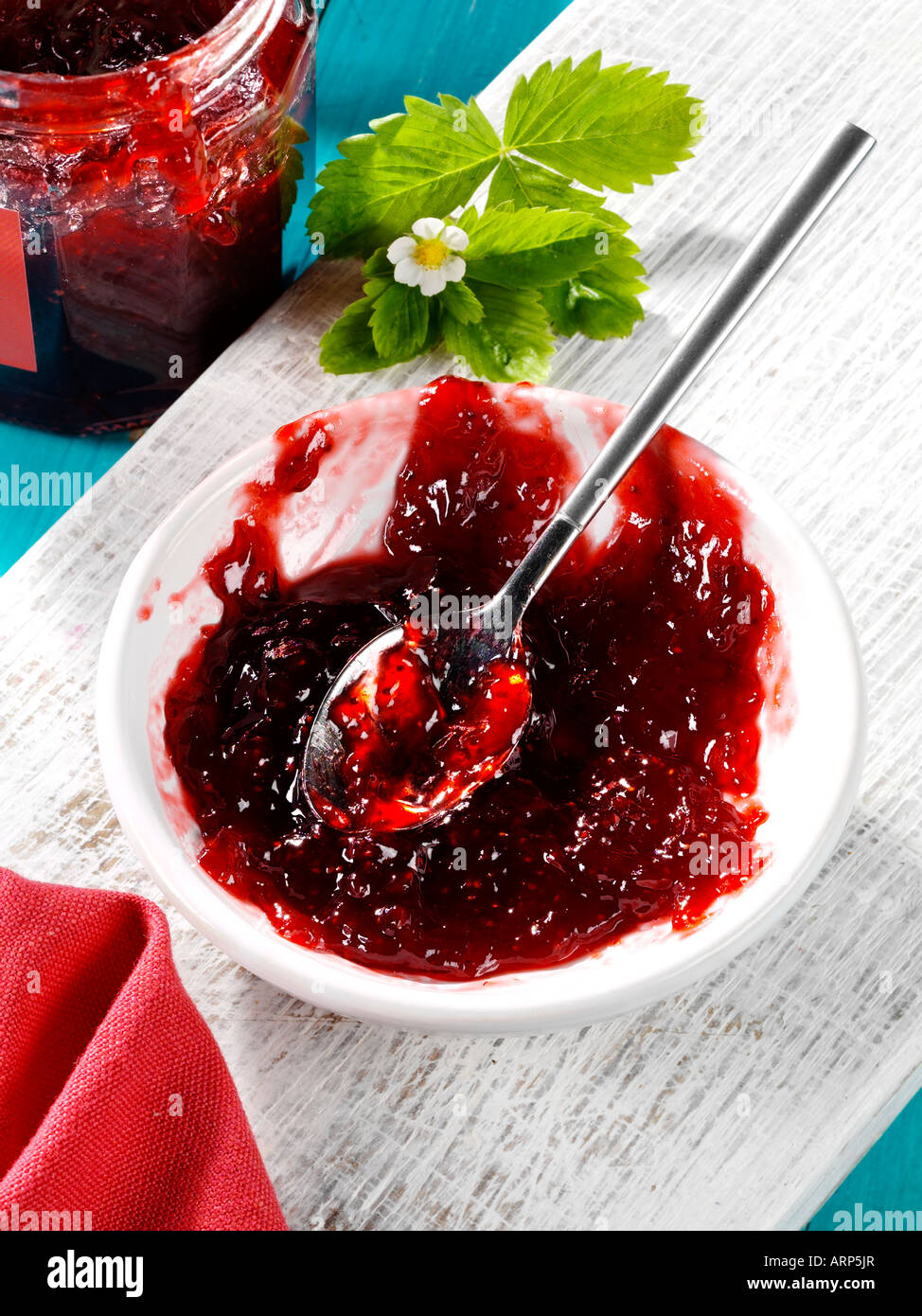 A small dish of strawberry jam with jar, strawberry leaves and ...