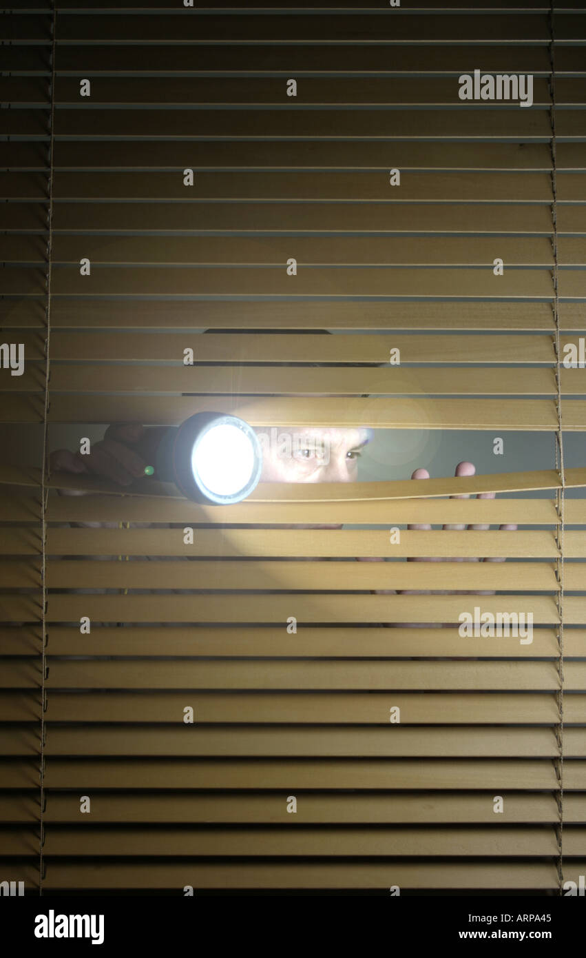 Man looks through window blind with torch on Stock Photo - Alamy