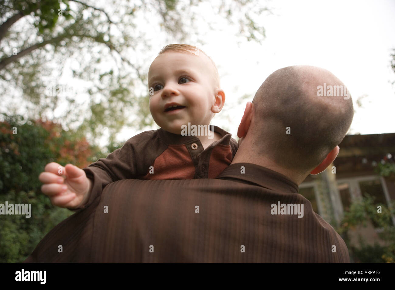 six month old infant boy peeking over father's shoulder, smiling ...